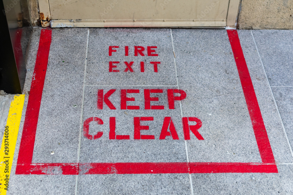 Fire Exit Keep Clear warning text and sign painted in red on concrete ...
