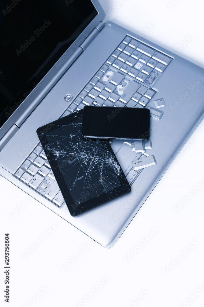A silver laptop with a broken keyboard, tablet with a cracked display ...