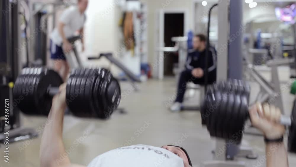 Bodybuilder trains pectoral muscles with a dumbbell while lying on a ...