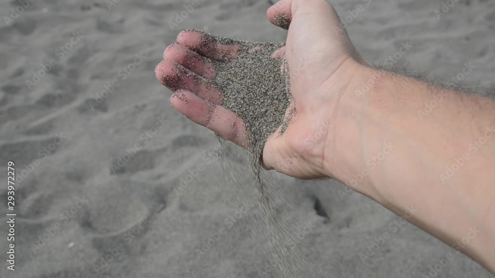 Gray sand falling down in a man's hand on the sandy beach at summer ...