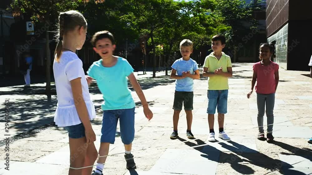 Happy children playing rubber band jumping game and laughing outdoors ...