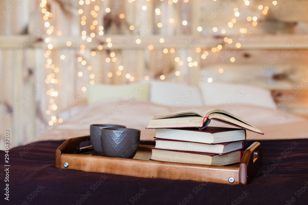 Stack of books and two cups of tea on a bed with background of lights ...