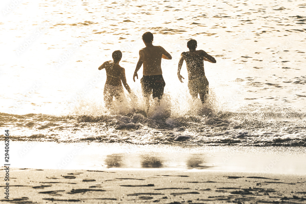 Teenagers running in the water of the ocean at sunset. Group of teen ...