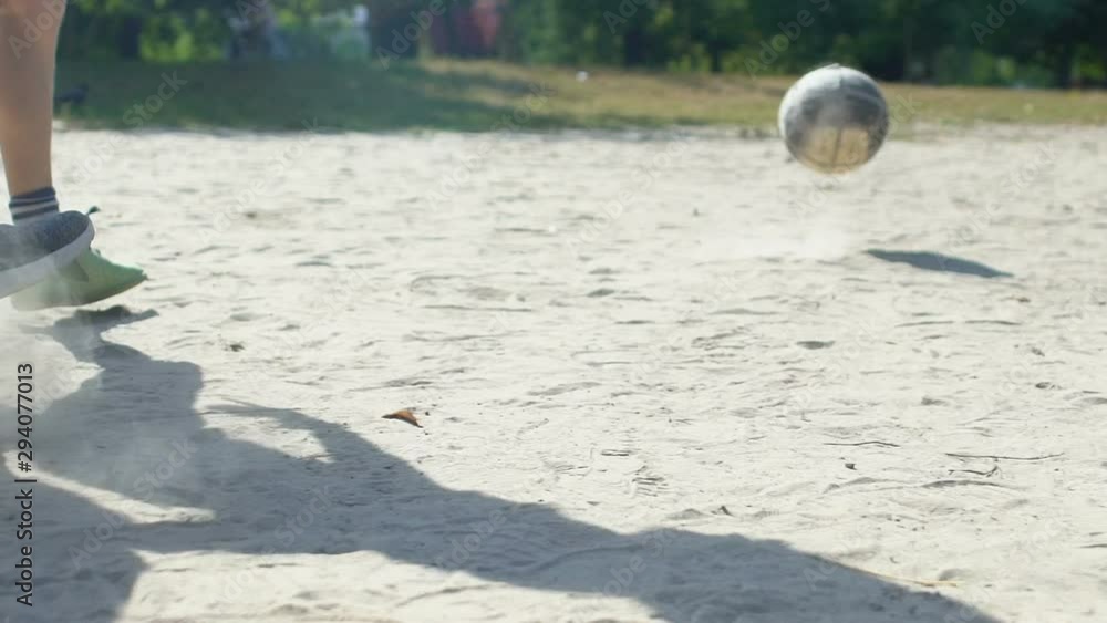 Schoolboys hitting football on dust ground playing street game, summer ...