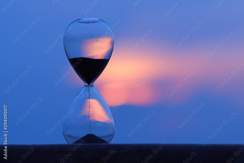 Falling sand in a hourglass at sunset sky background. Stock Photo ...