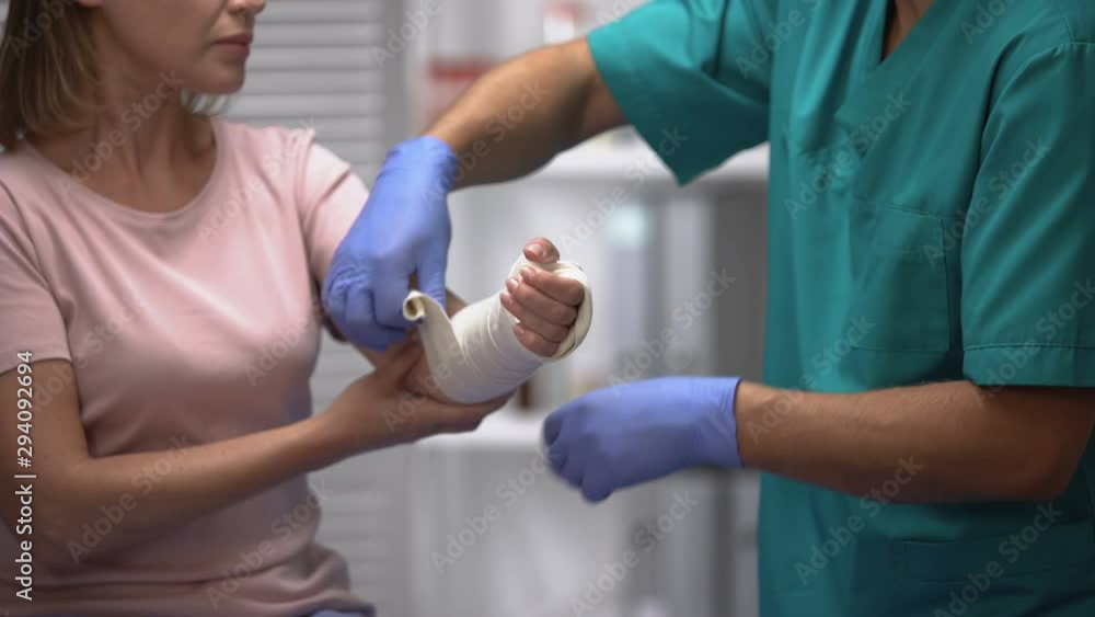 Surgeon applying elastic wrap on female patient arm, rehabilitation ...