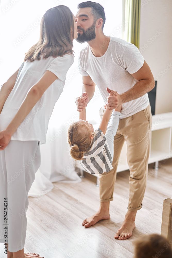 two parents kissing each other whle their child climbing to the father ...