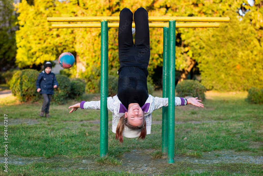 Teen girl doing yoga outdoors, hanging upside down on a horizontal bar ...