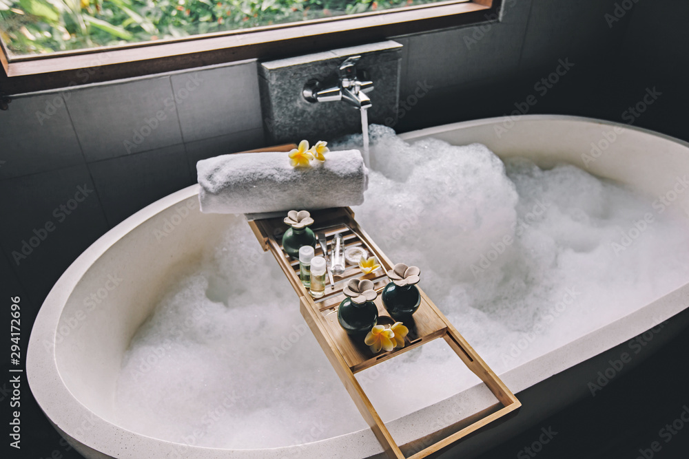 Bath with foam is filling with water, beauty products on bathtub. Stock ...