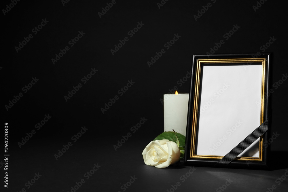 Funeral photo frame with ribbon, white rose and candle on dark table ...