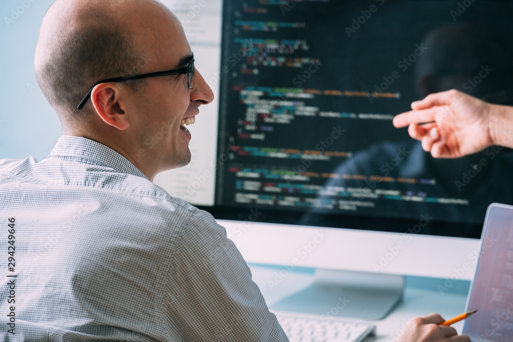 Programmer, working behind the desk, analysing code while chatting with ...