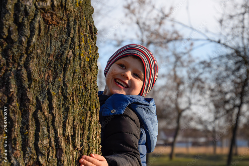 little boy is hiding behind a big tree. A child peeks out from behind a ...