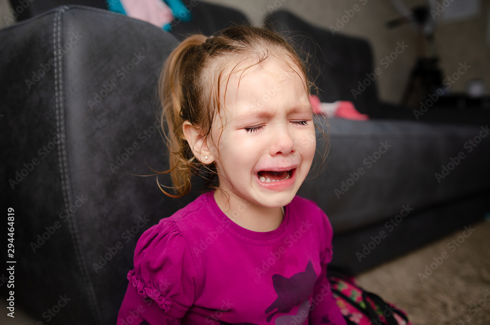 Little girl sitting on the floor, she is upset and crying. The child is ...