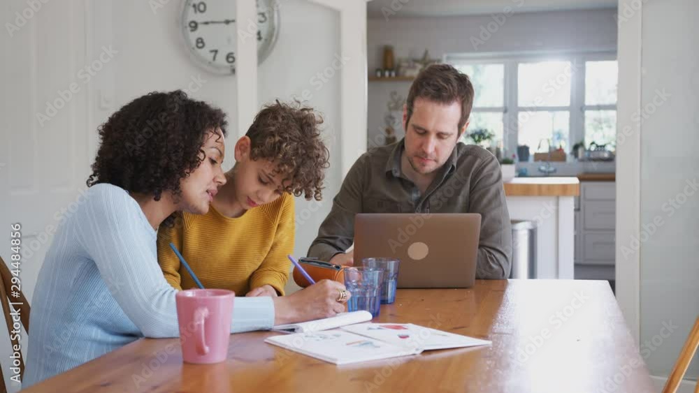 Father Works On Laptop As Mother Helps Son With Homework On Kitchen ... Father Works On Laptop As Mother Helps Son With Homework On Kitchen ...