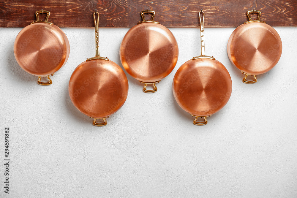 Row of shiny clean copper pans, different size, hung on wooden plank ...
