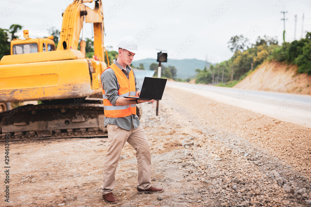 Caucasian handsome engineer using a laptop on road construction site ...
