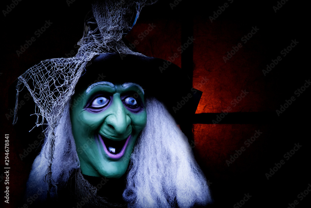 Scary halloween witch standing near window of the spooky house with red ...