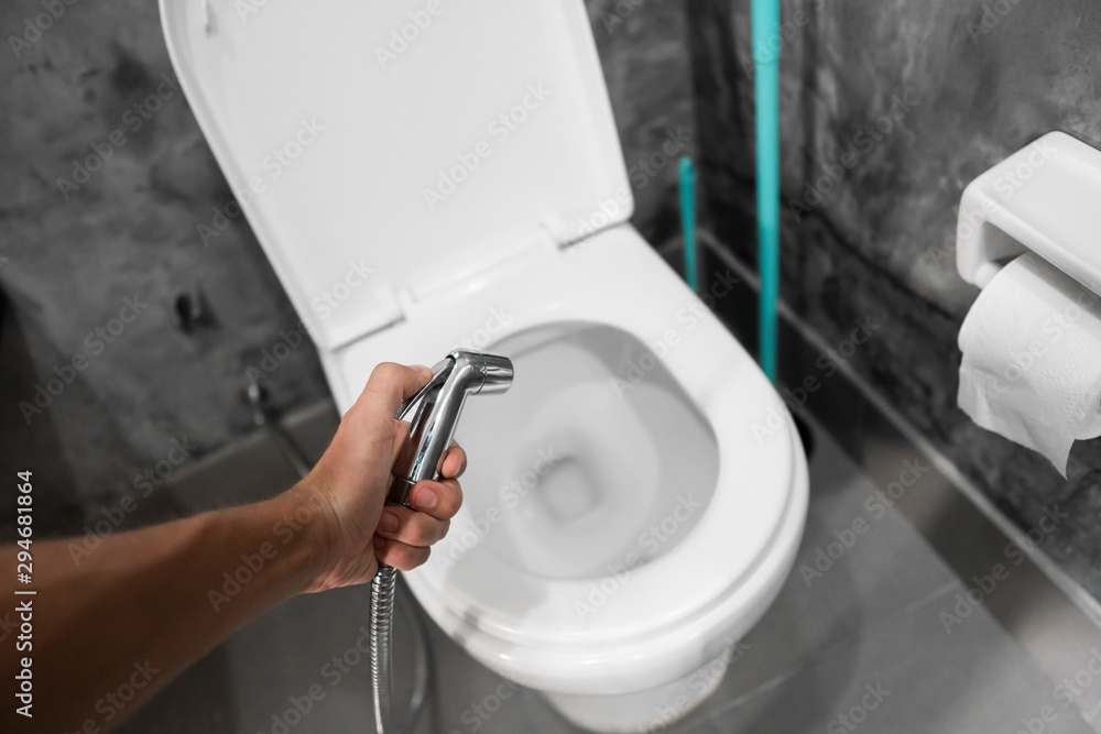 Using of bidet shower with a white toilet. Bidet shower in male hand ...