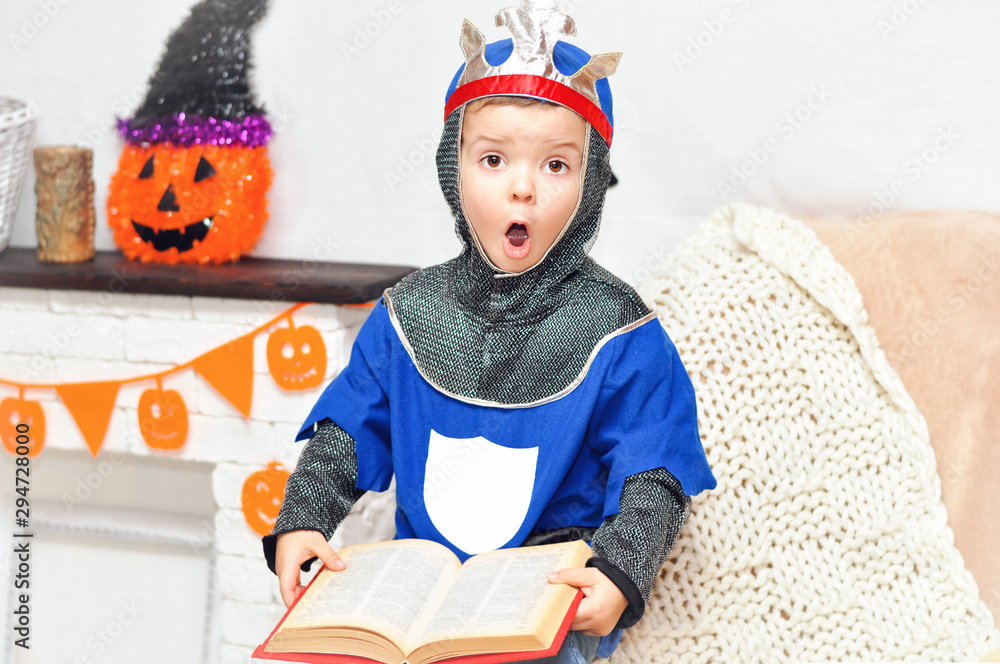 Little surprised boy in a knight costume with a crown on his head sits ...