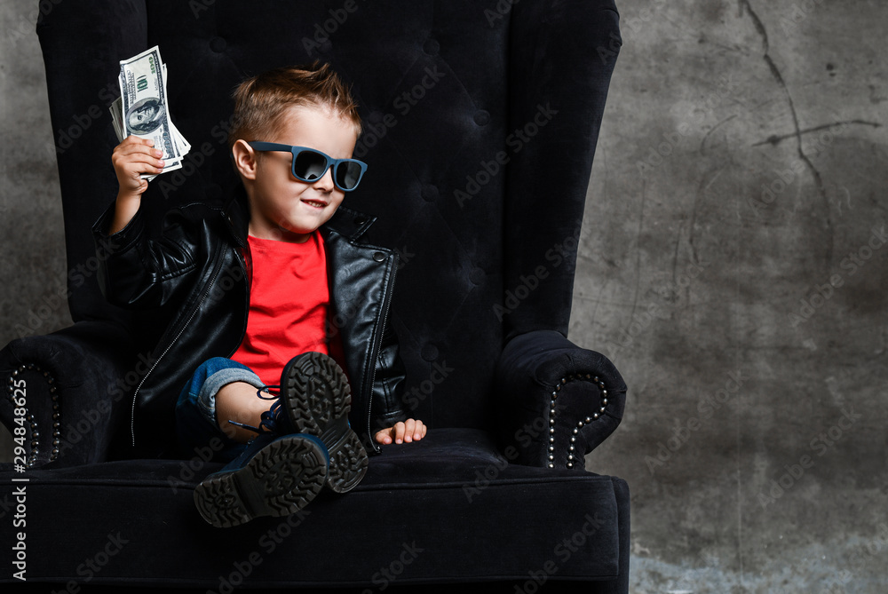 Stylish rich kid boy in leather jacket and red t-shirt is sitting in ...