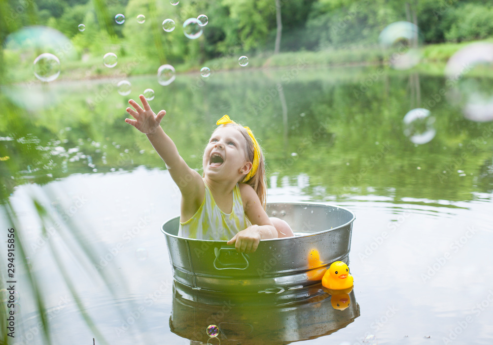 Happy kid sitting in tub touching soap sud over her. Little girl having ...