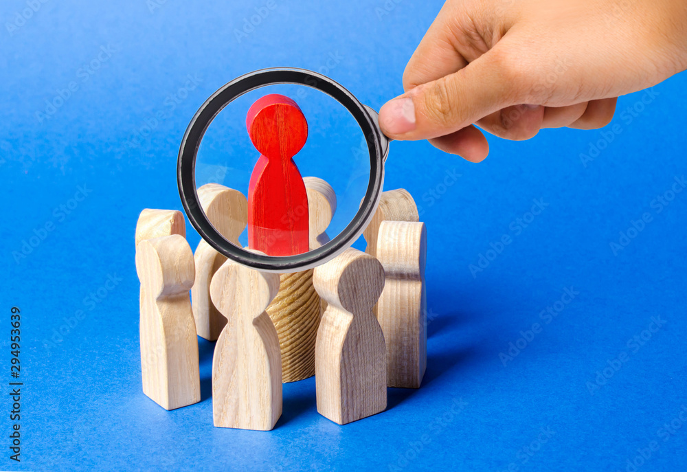 A magnifying glass looks at a red figure of the leader in the center of ...