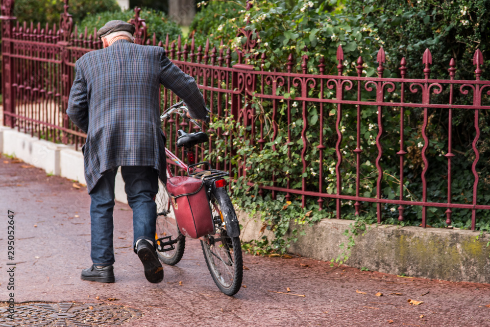 un vieillard vieux homme pousse son vélo dans la rue Photos | Adobe Stock