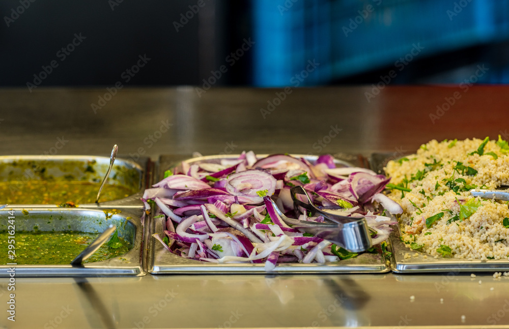 ingredients at a falafel bar with metal vegetable tongs onions, sauce ...