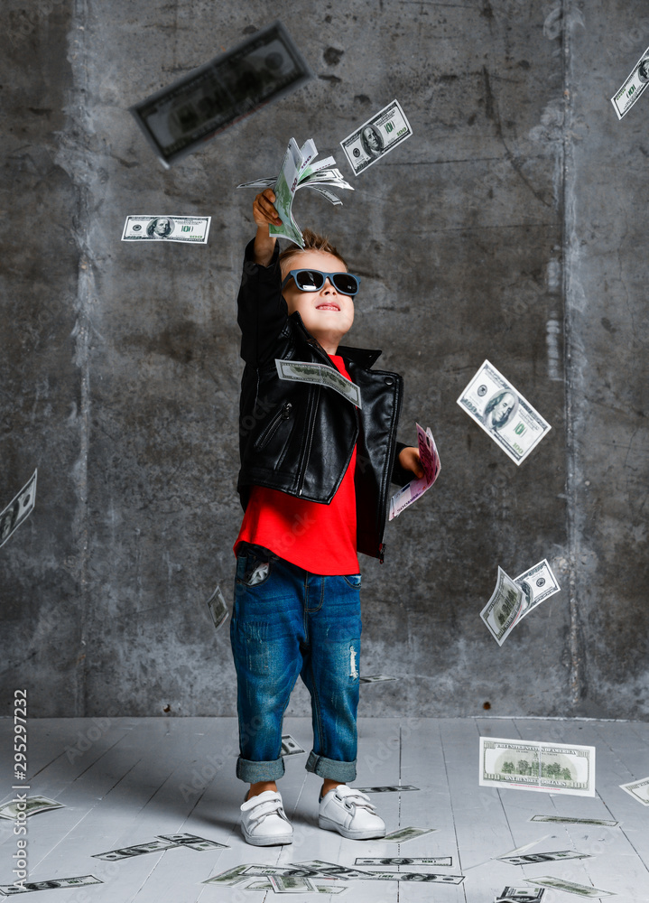 Smiling rich kid boy in sunglasses, leather jacket and blue jeans is ...