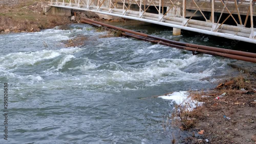 Vidéo Stock Rapid flow of river under bridge in city, rusty pipes laid ...