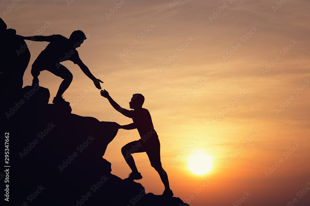 Silhouette of people helping each other hike up a mountain at sunset ...