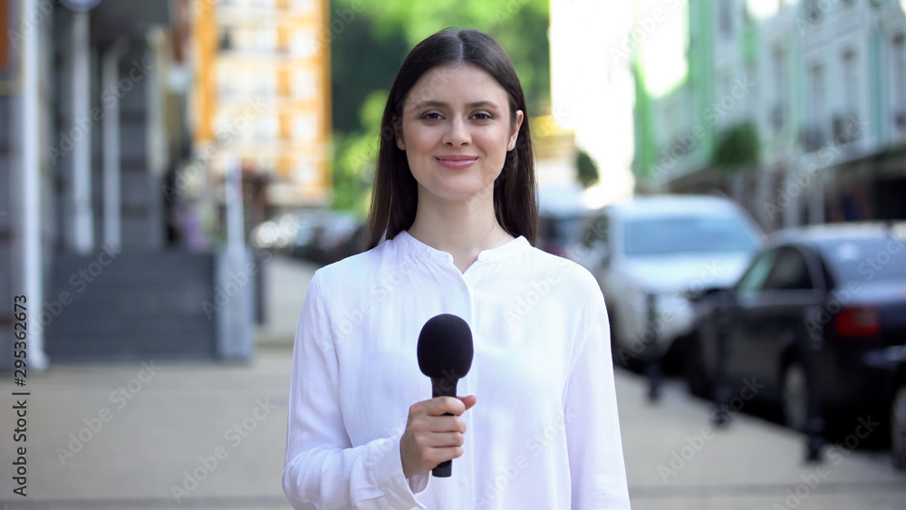 Cheerful female reporter holding microphone and smiling at camera ...
