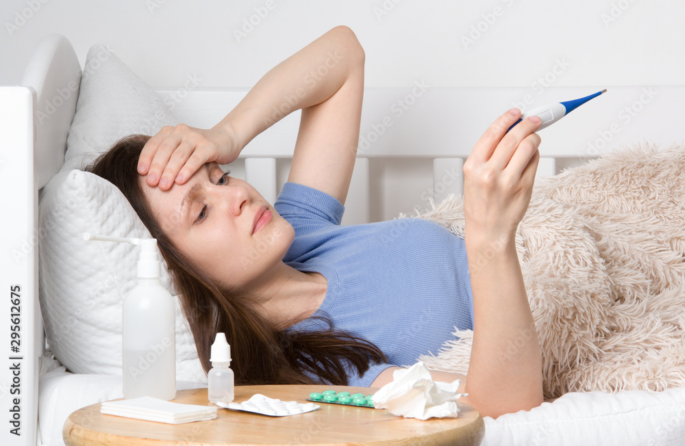 Sad Girl with fever measuring her body temperature lying on a bed at ...