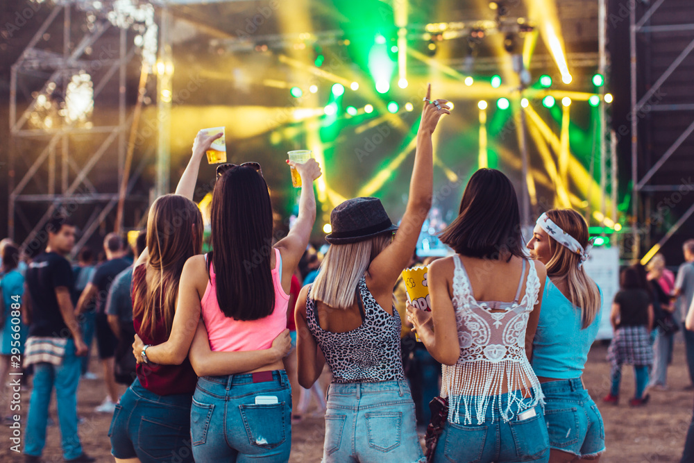 Back view of group of female friends at music festival drinking beer ...