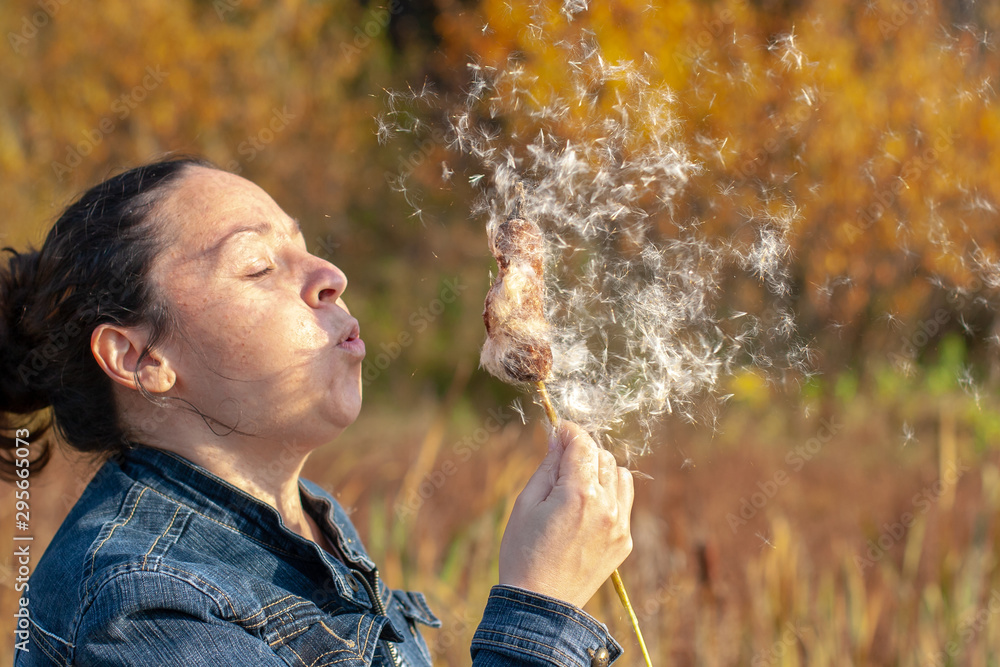Girl with pouting cheeks closing her eyes blows on a cattail in her ...