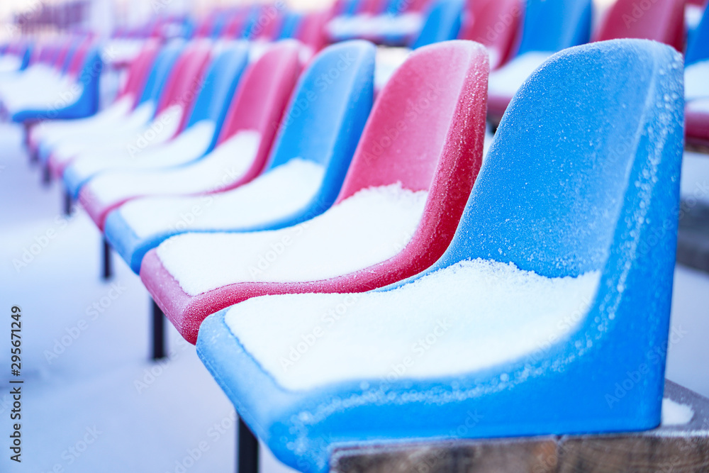 Snow-covered multi-colored seats in the stadium in winter. Snowfall ...