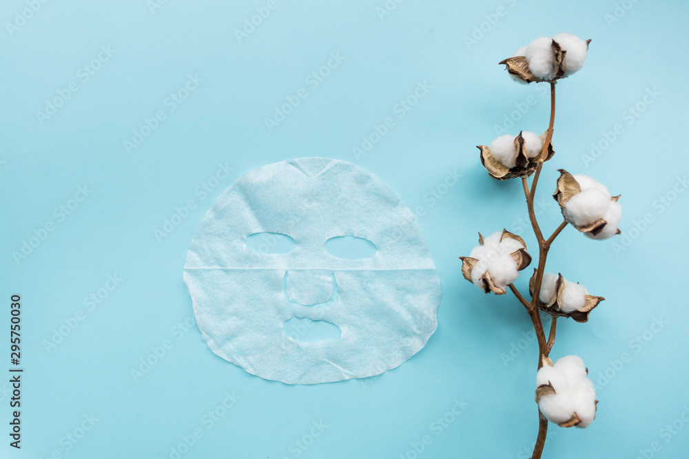 Sheet facial mask and cotton flower on pastel blue paper background ...