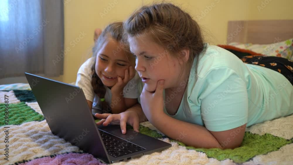 Girls of seven and twelve years old work on a laptop in the room, lying ...