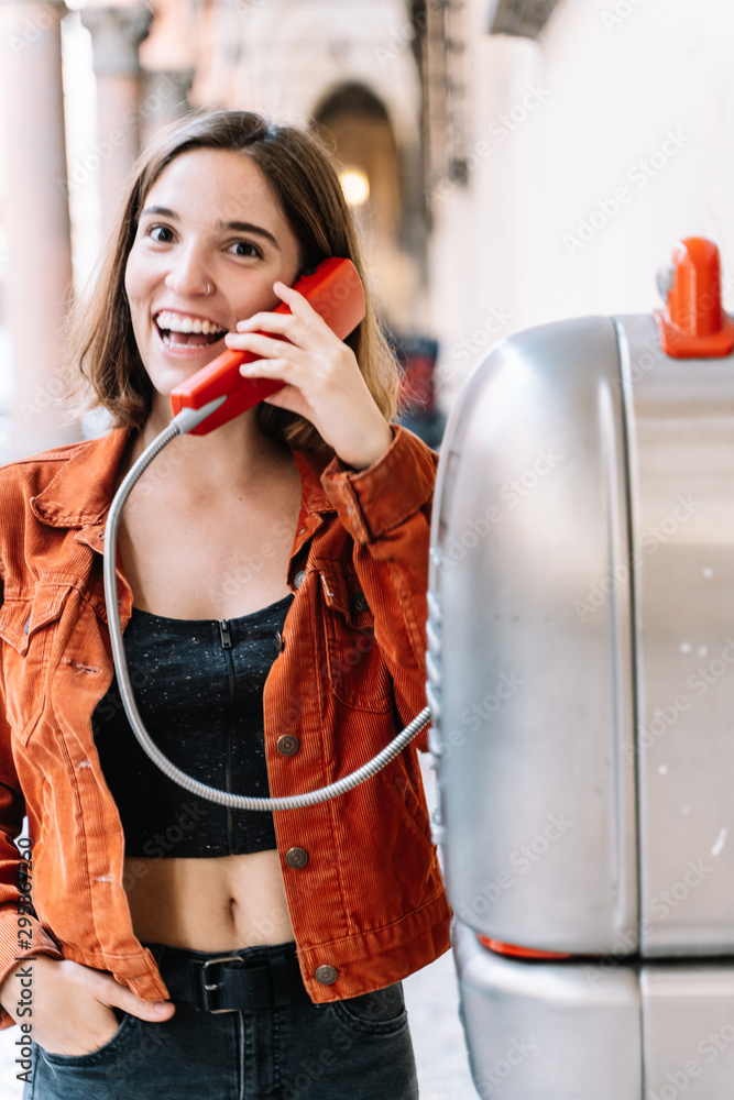 Vertical photo of a girl with an orange jacket calling through a phone ...