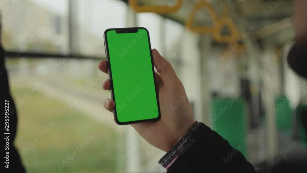 Hands uses holding a mobile telephone with a vertical green screen background tram seat people ...