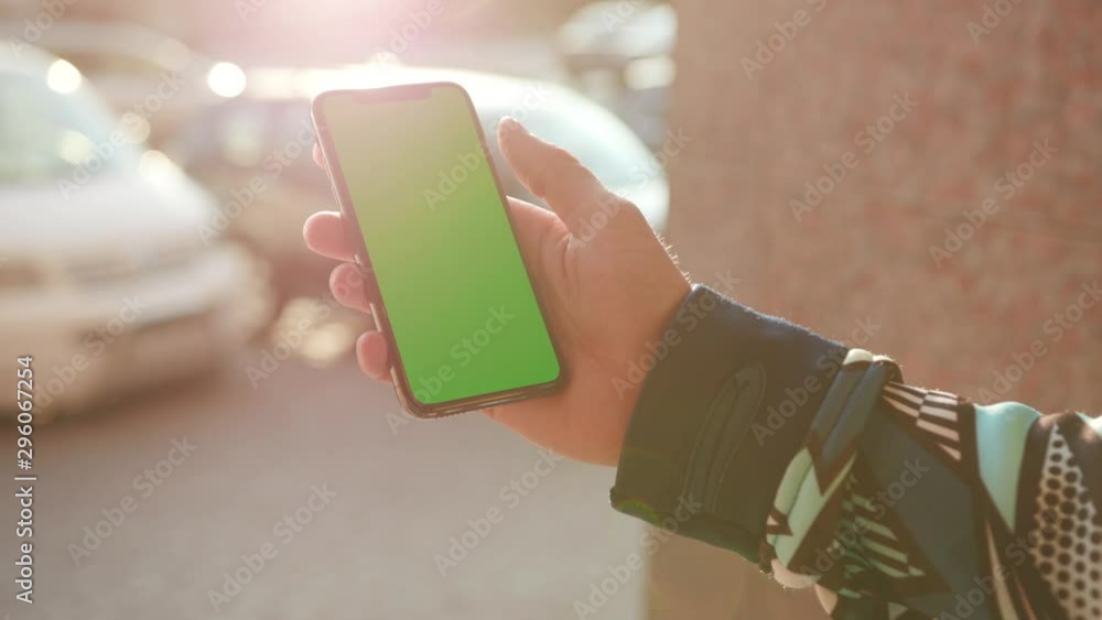 Young man hand using phone with vertical green screen background sunlight street people city ...