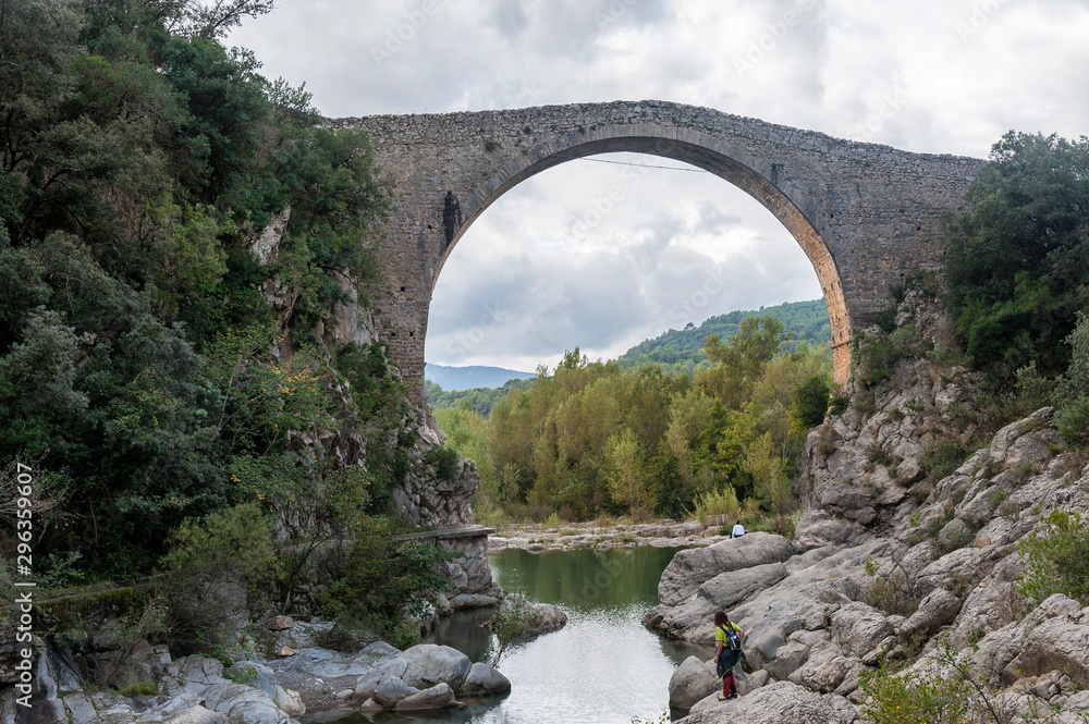 A young hiker contemplates the old medieval bridge of Llierca, in the ...