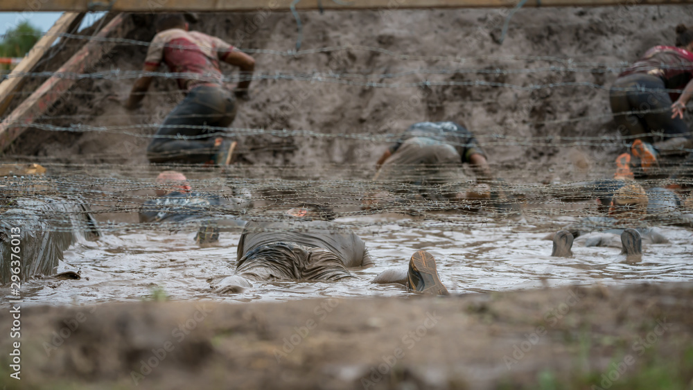 People crawling in mud under barbed wire at an obstacle course race ...