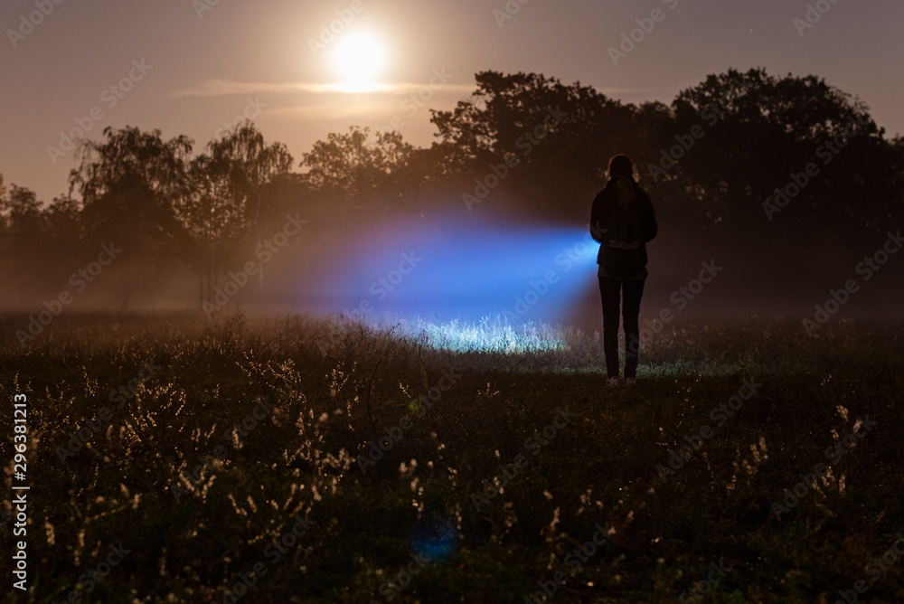 A person with a flashlight on a foggy meadow, with a flashlight in the ...