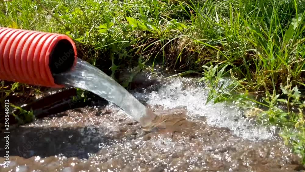 water from a red corrugated pipe flows down the drain. Water is flowing ...