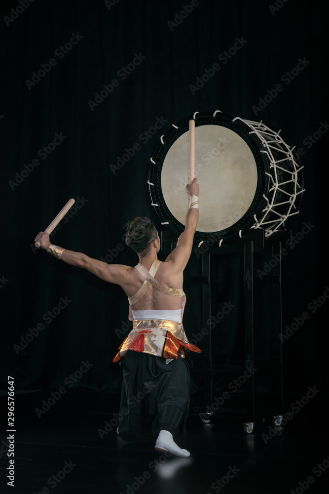 Taiko drummer hits the big drum on stage on a black background, back ...