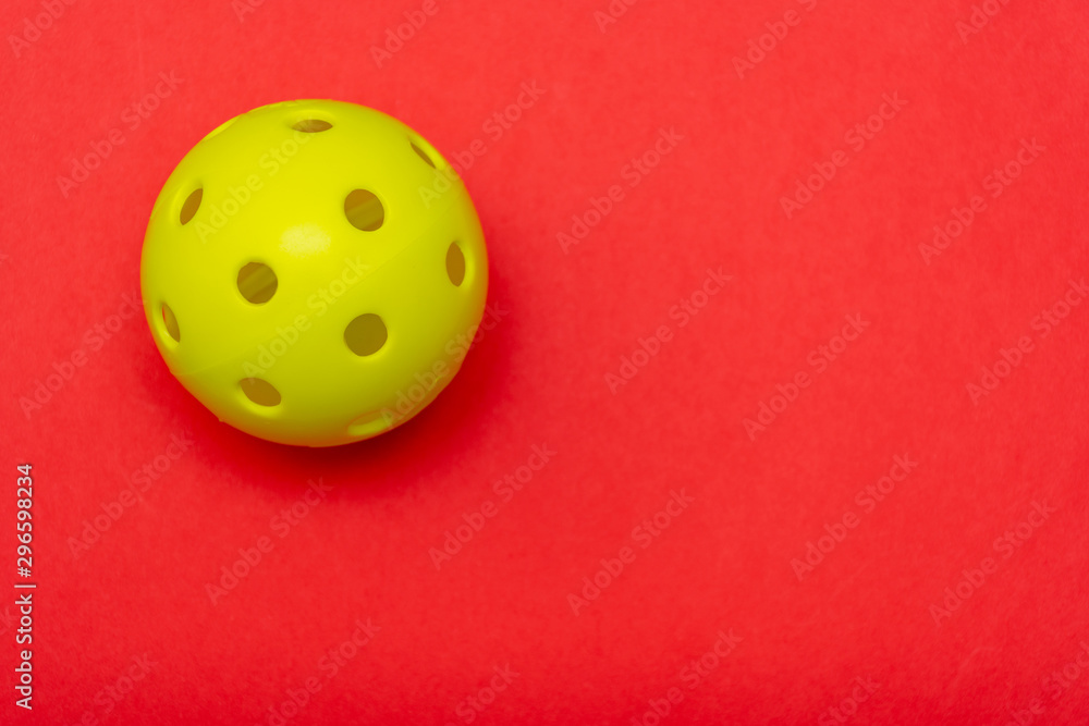 Bright yellow pickleball or whiffle ball on a solid bright red flat lay ...
