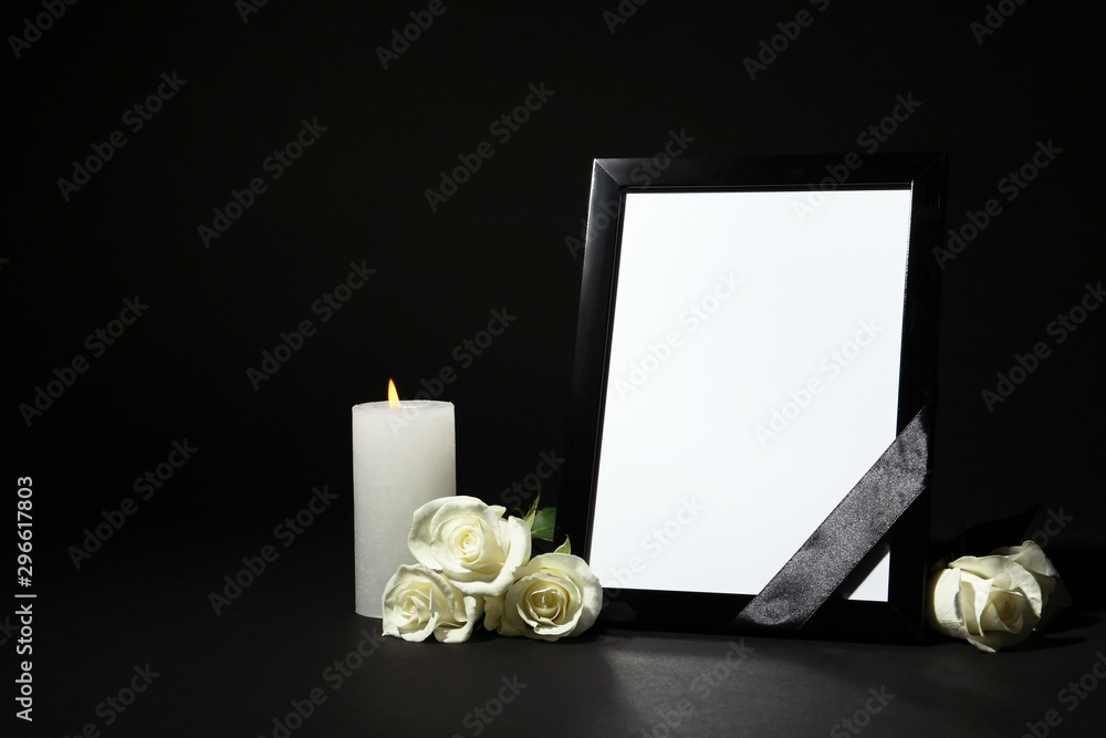 Funeral photo frame with ribbon, white roses and candle on dark table ...