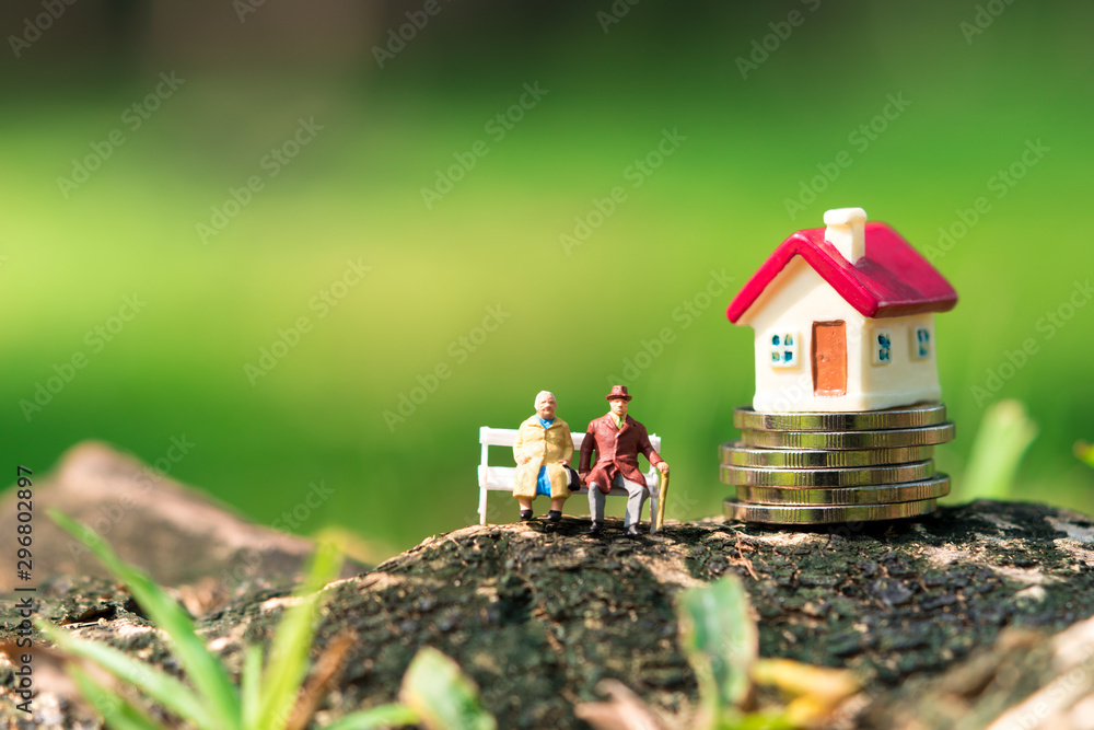 Miniature elderly people sitting with mini house on stack coins using ...