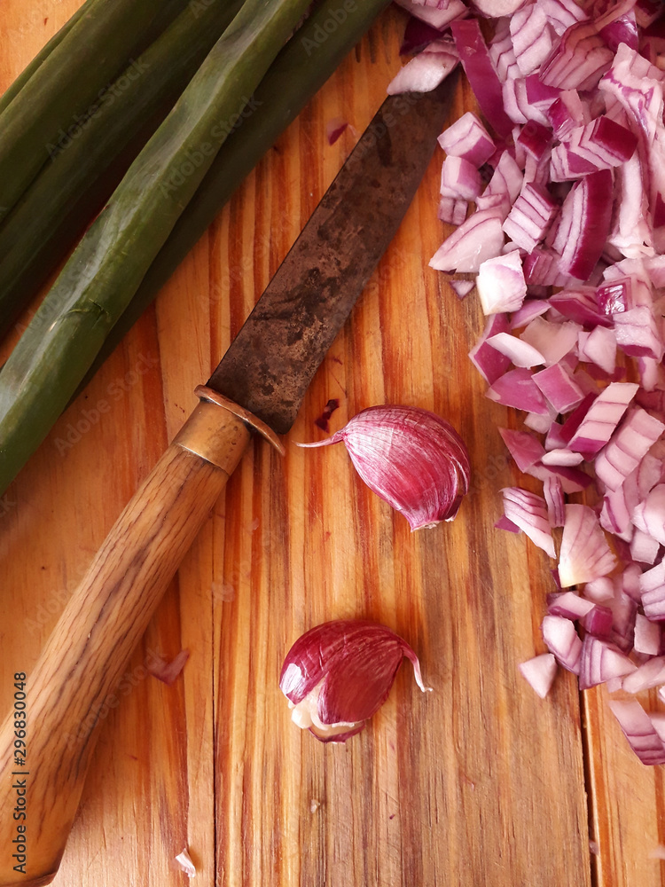 cebolla roja con dos ajos morados y un cuchillo rústico sobre tabla de ...